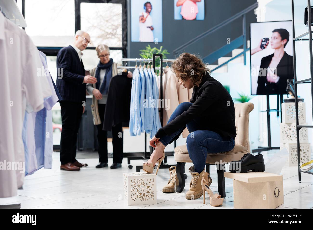 Stylish customer sitting on chair trying elegant shoes, shopping for trendy merchandise to ...