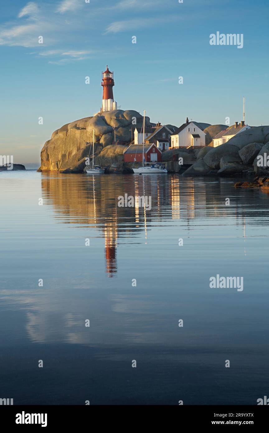 Lighthouse on cliff at a distance with reflection in calm and peaceful ...