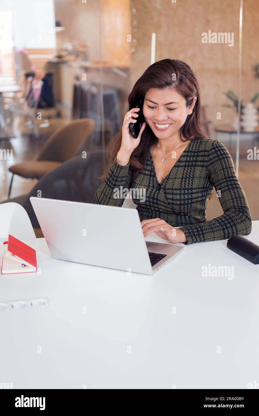 Happy lady receiving phone call while using netbook Stock Photo - Alamy