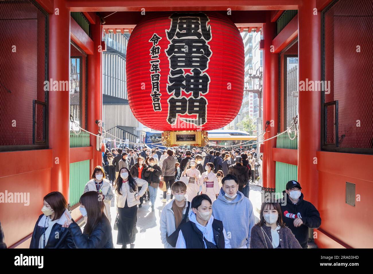 Crowd of people walking through a traditional Japanese gate with a large red lantern, the ...