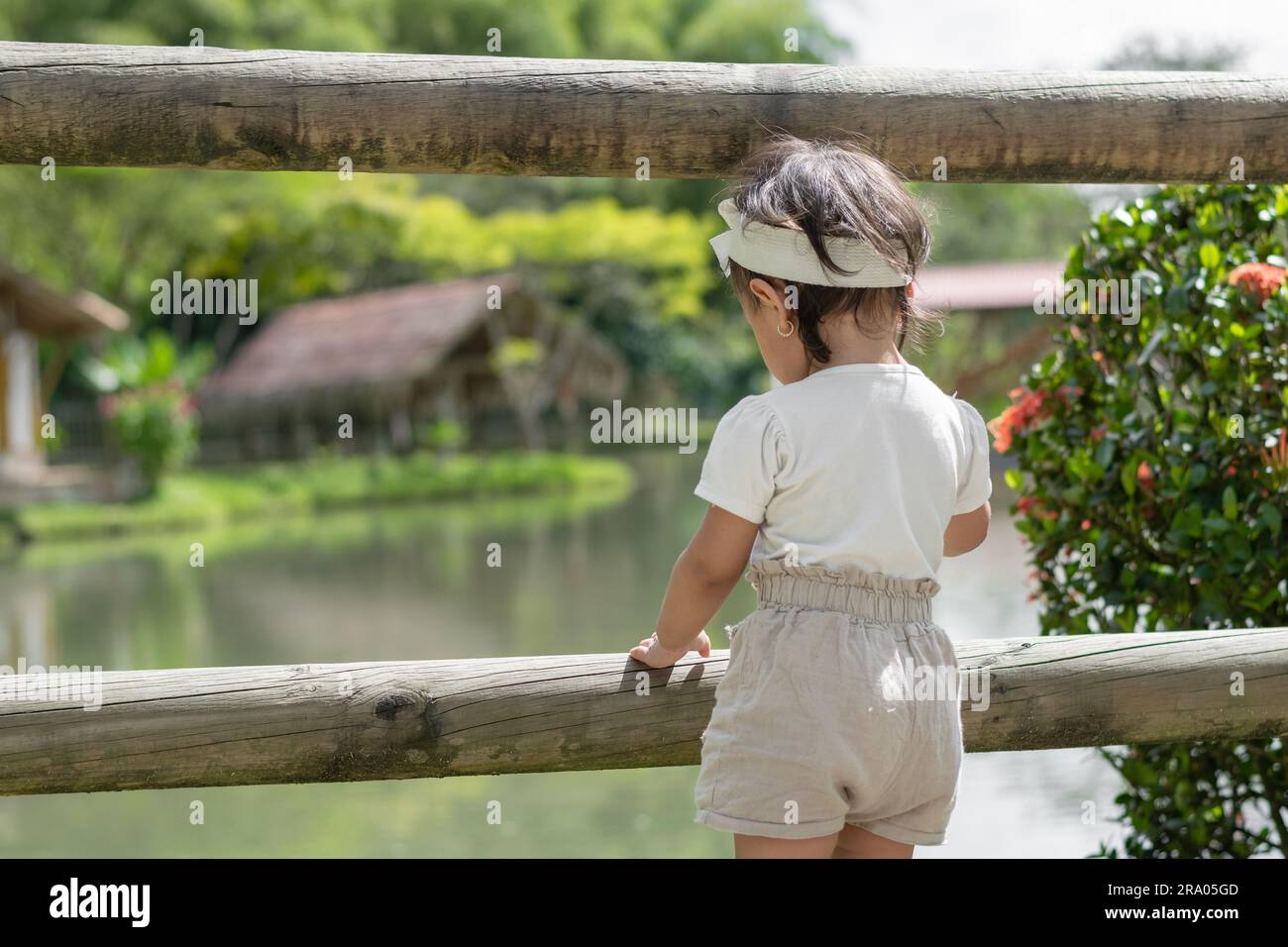little latina girl standing next to the wooden fence looking very ...