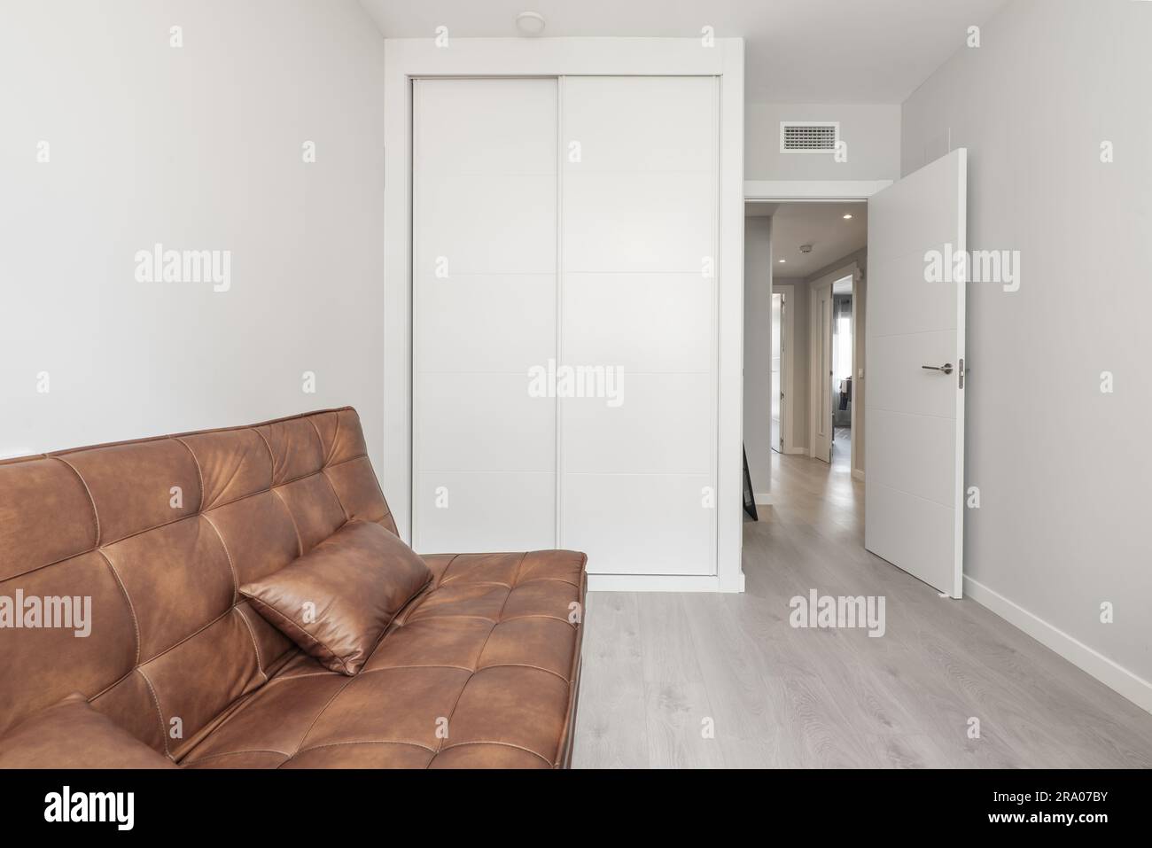 Room with brown leather folding sofa bed and a built-in wardrobe with ...