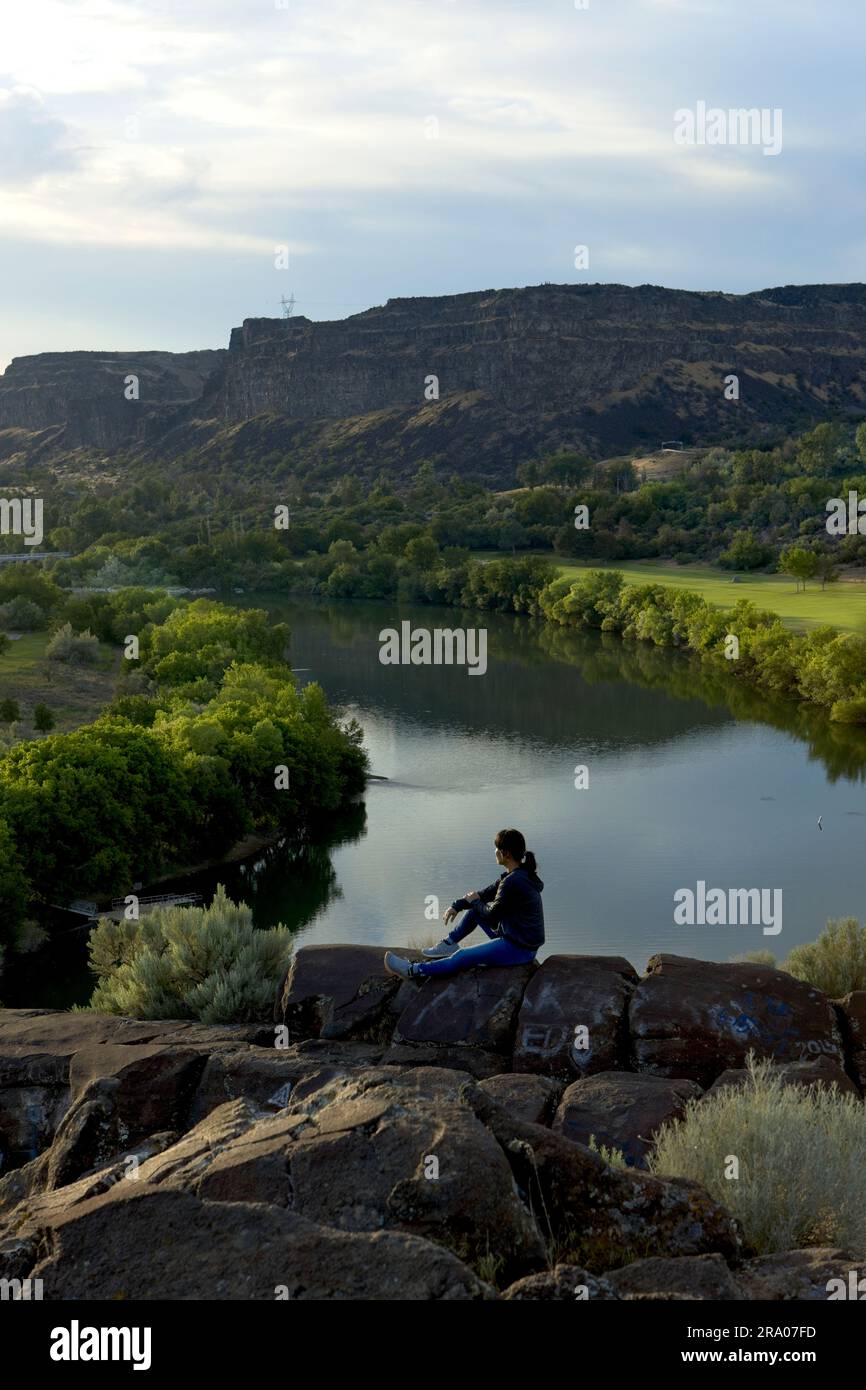 A woman sits above the water looking out at the beautiful scenery of ...