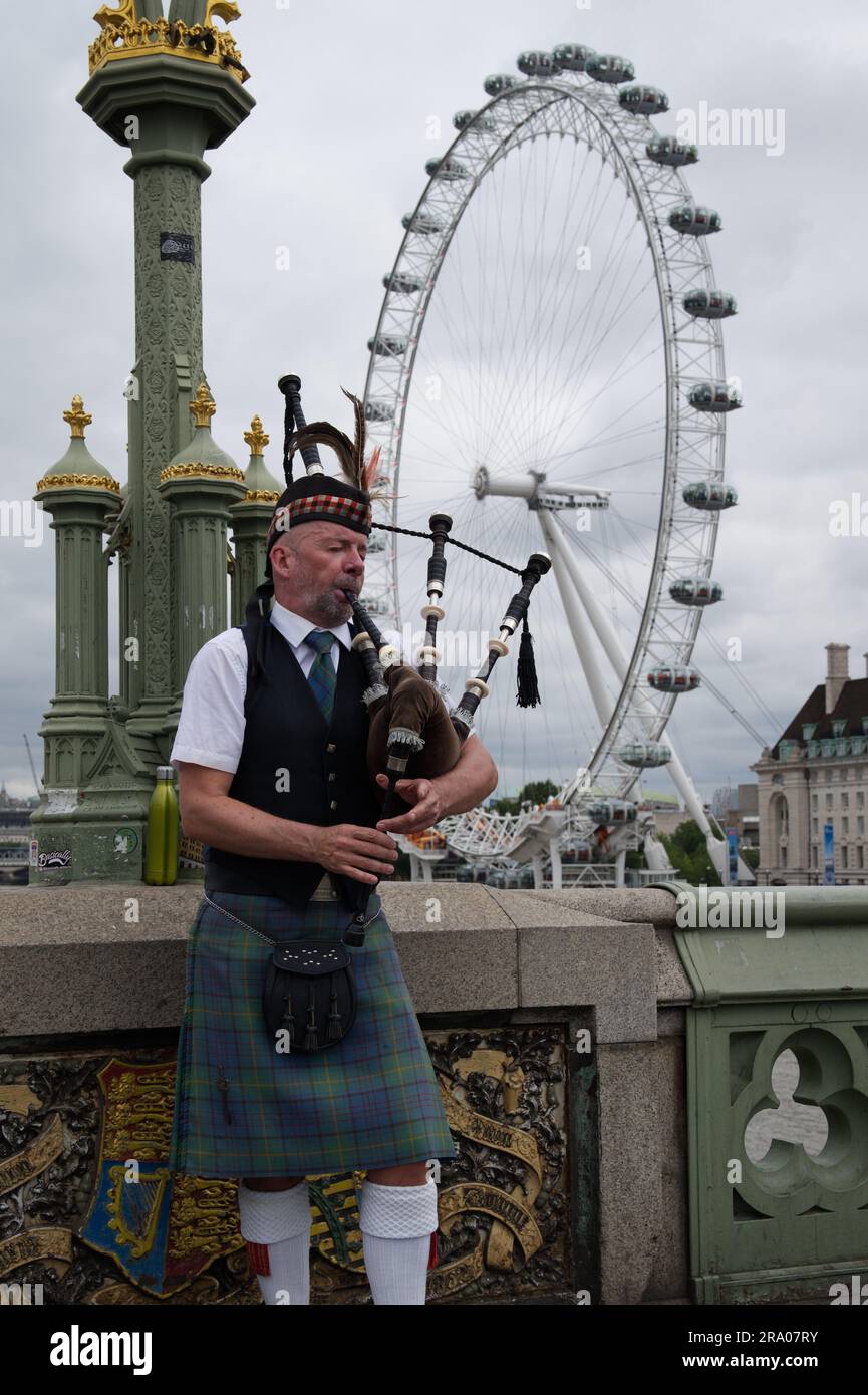 A bagpiper busking on Westminster bridge with the London Eye in the ...