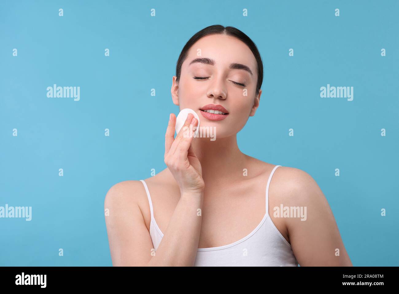 Beautiful woman removing makeup with cotton pad on light blue ...