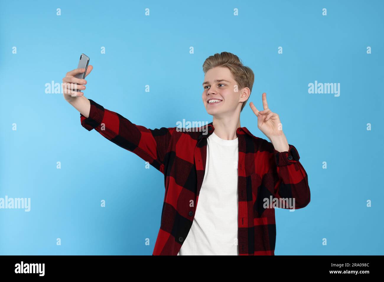 Teenage boy taking selfie on light blue background Stock Photo - Alamy