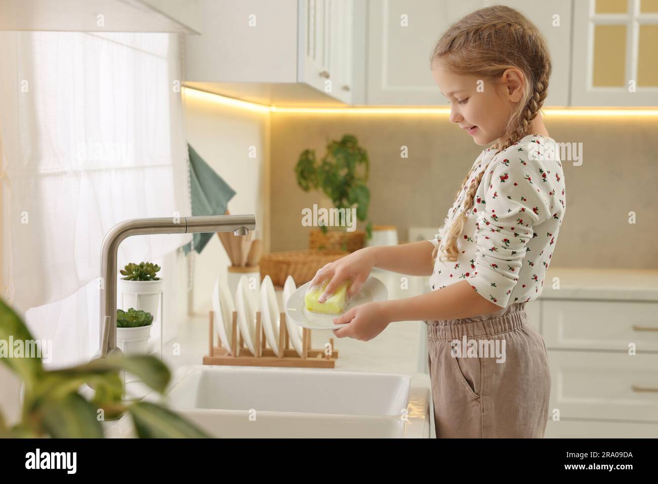 Little girl washing plate above sink in kitchen Stock Photo - Alamy