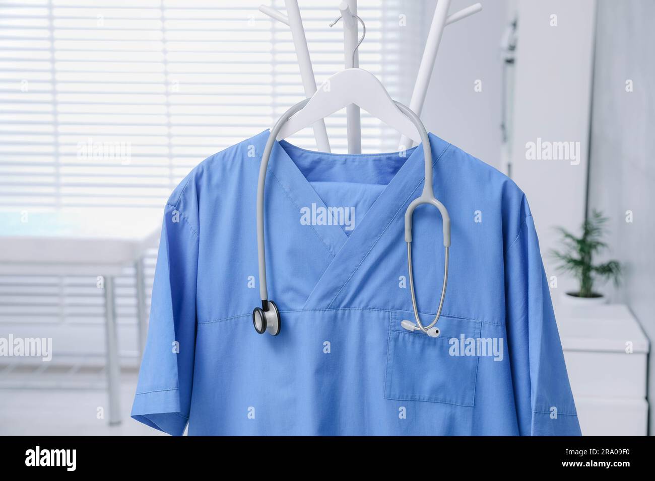 Blue medical uniform and stethoscope hanging on rack in clinic, closeup ...
