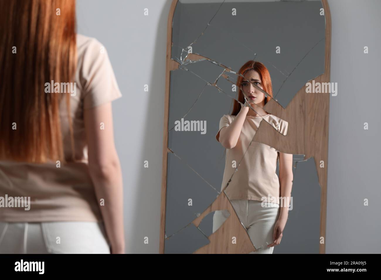 Mental problems. Depressed woman reflecting in broken mirror indoors ...