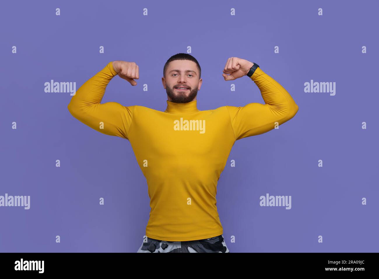 Handsome man showing muscles on purple background Stock Photo - Alamy