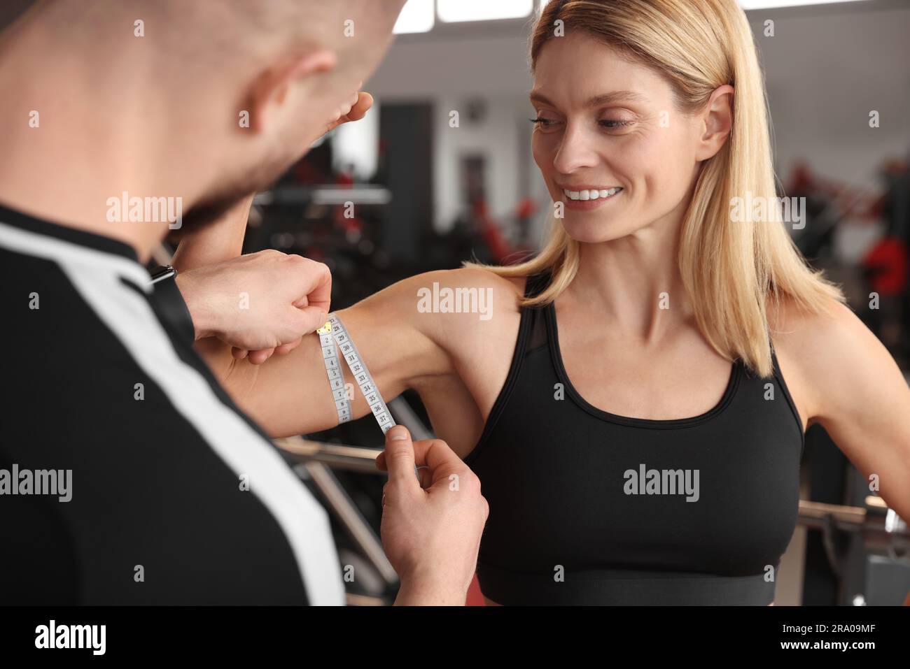 Trainer measuring woman`s biceps with tape in gym Stock Photo - Alamy