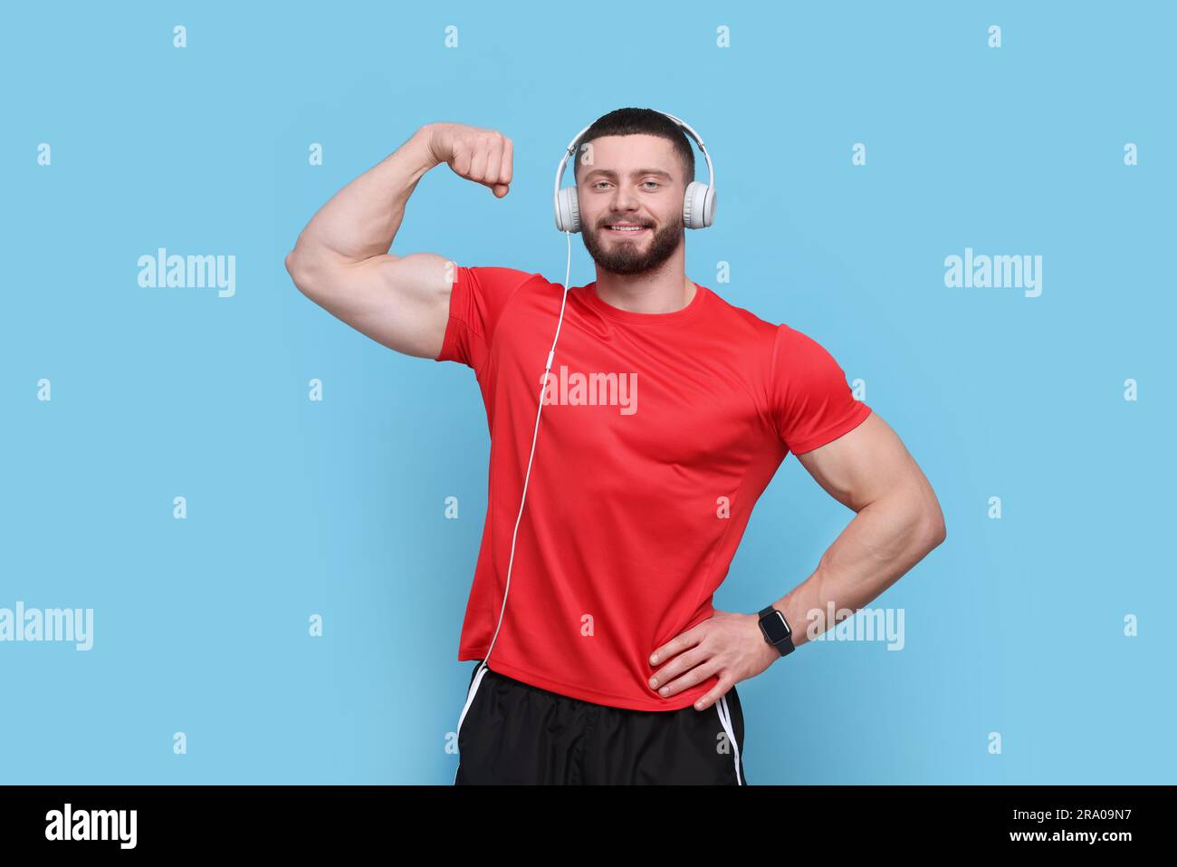 Handsome man with headphones showing muscles on light blue background ...