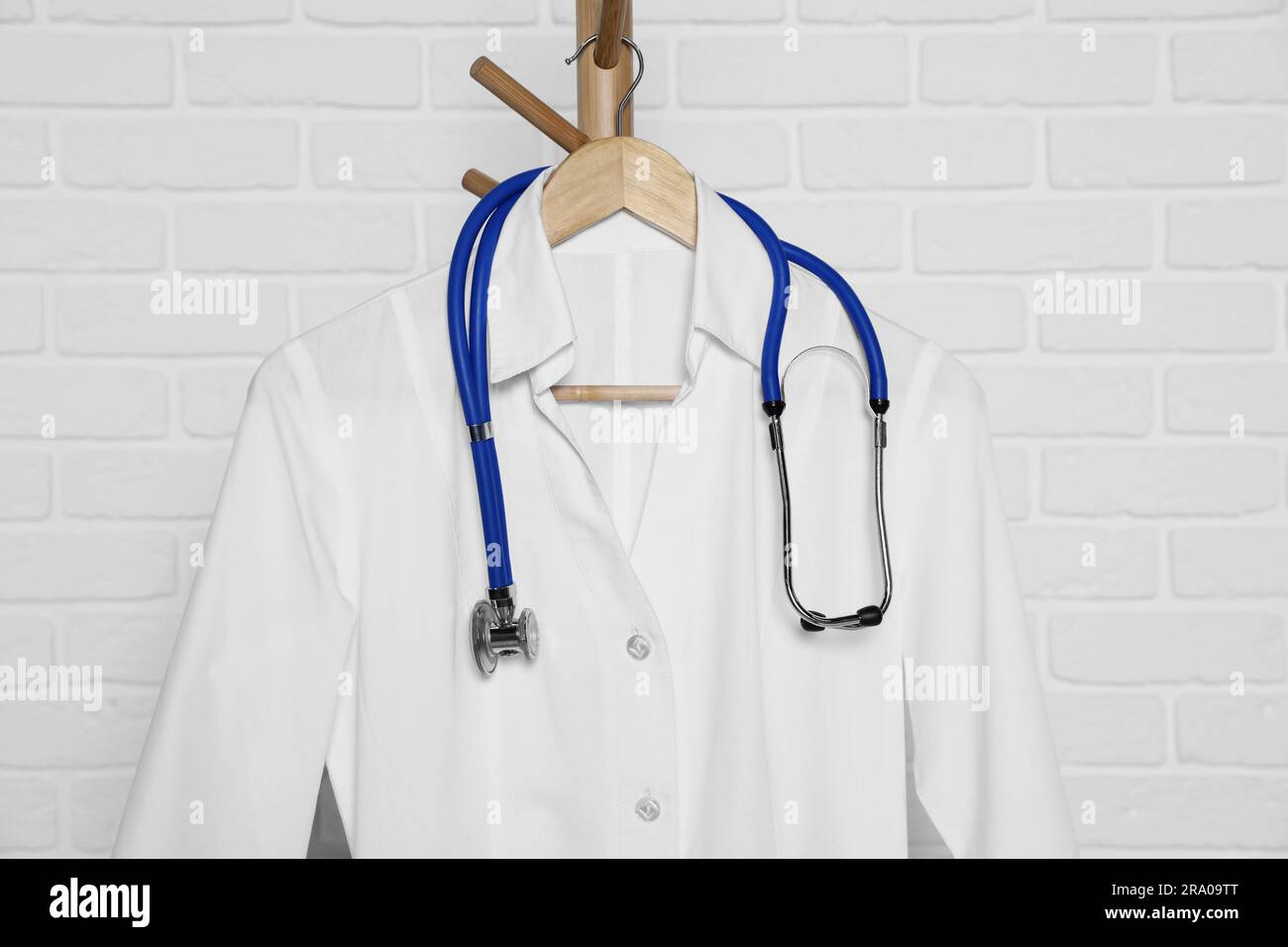 Medical uniform and stethoscope hanging on rack near white brick wall ...