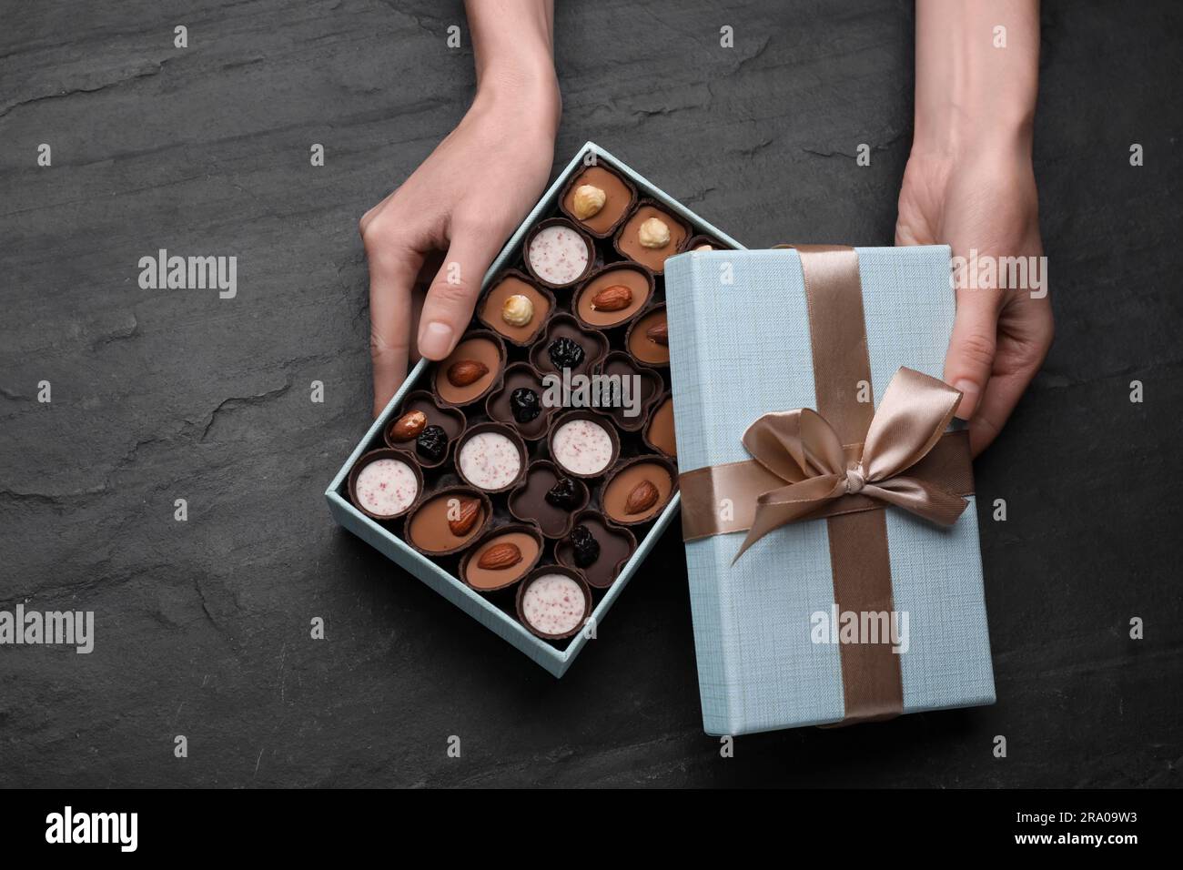 Woman with open box of delicious chocolate candies at black table, top ...