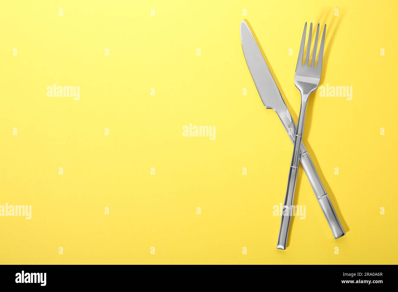 Shiny fork and knife on yellow background, flat lay. Space for text ...