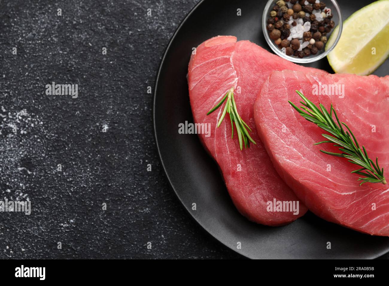 Raw tuna fillets with rosemary on black table, top view. Space for text ...