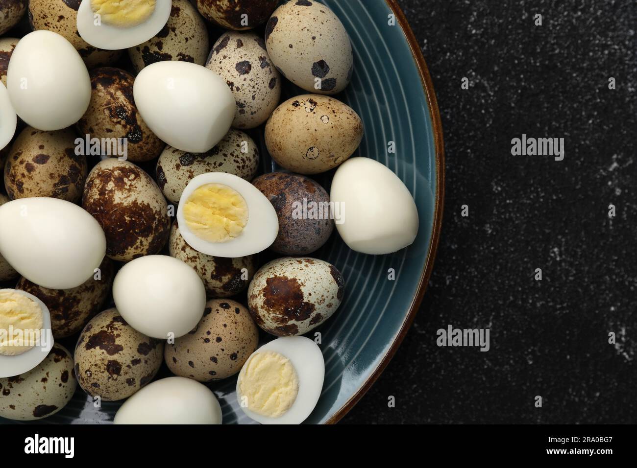 Peeled and unpeeled hard boiled quail eggs in plate on black table, top ...