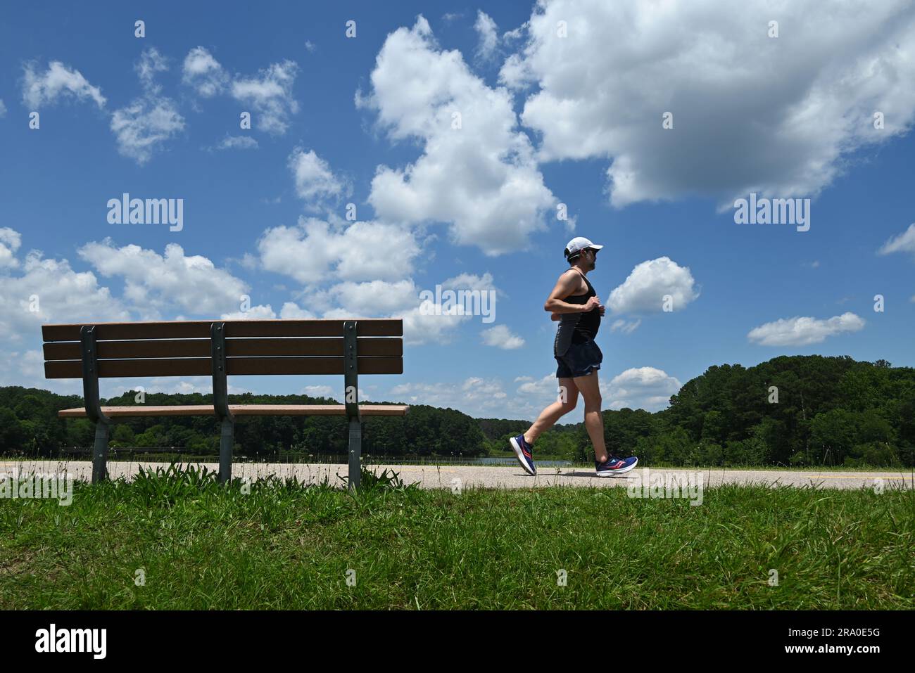A man jogs past a park bench with a blue sky background in Raleigh, NC ...