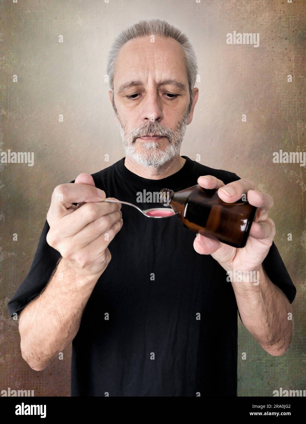 A mature man is pouring cough syrup in a spoon to cure his sore throat ...