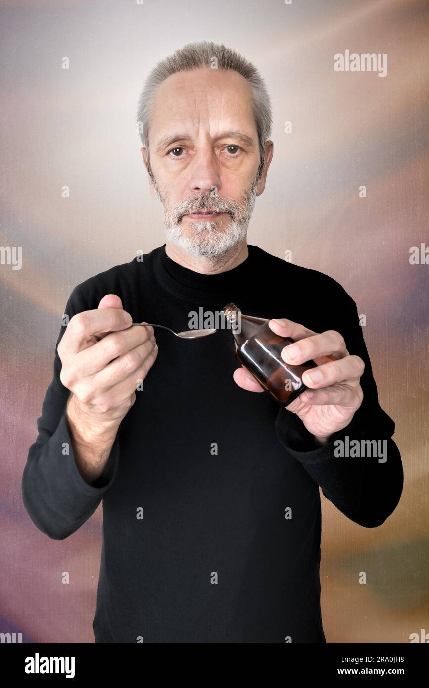 A mature man is pouring cough syrup in a spoon to cure his sore throat ...