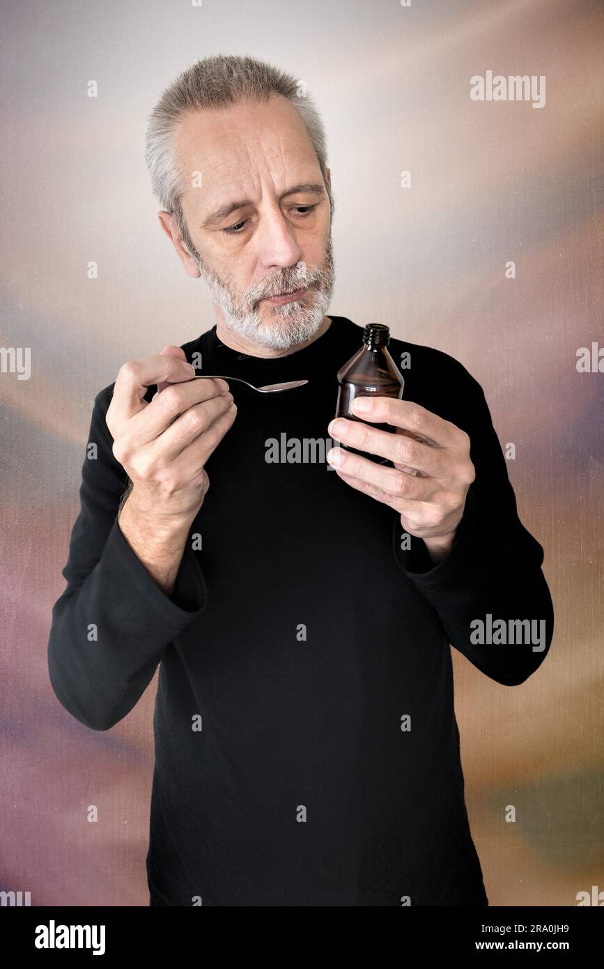 A Mature Man Is Reading The Label Of A Cough Syrup Bottle Before To