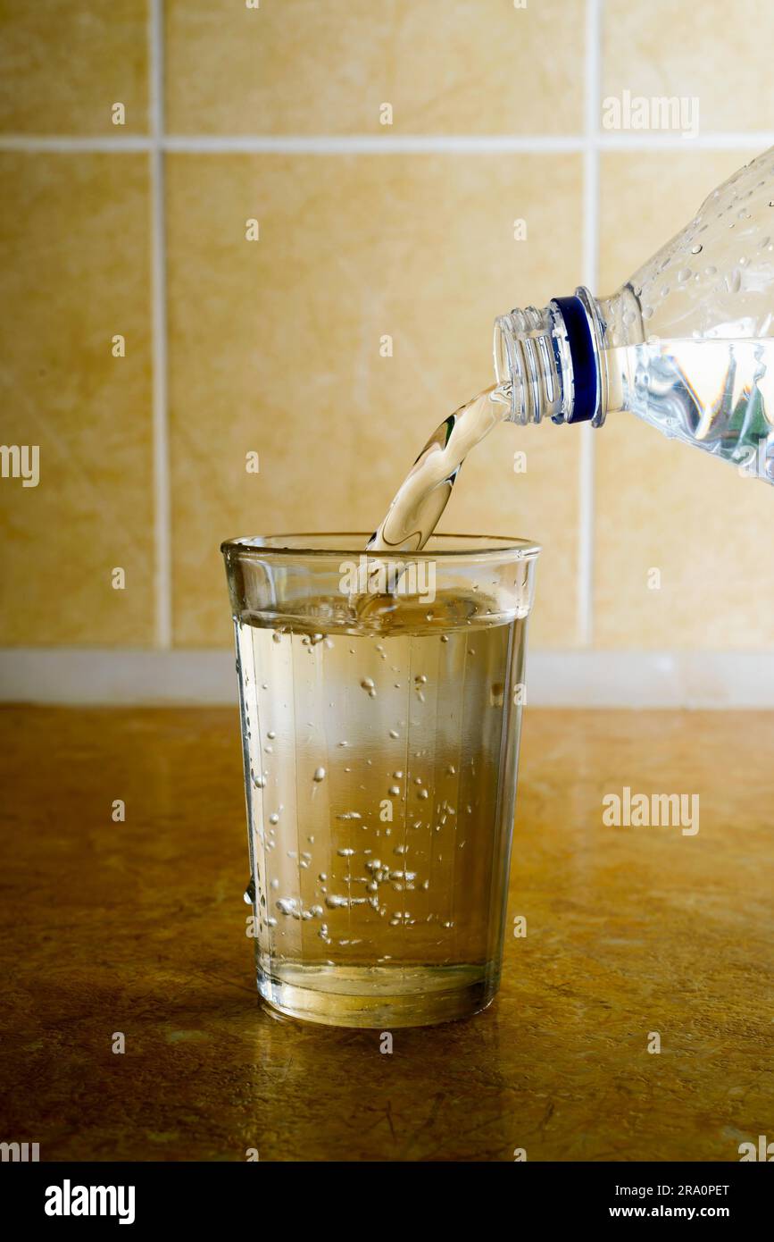 Pouring fresh mineral water from a plastic bottle into a simple glass in kitchen Stock Photo - Alamy