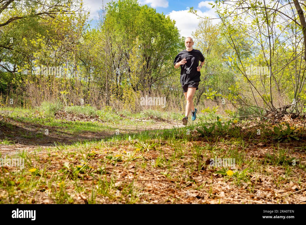 A senior man dressed in black is running in the forest, during a warm ...