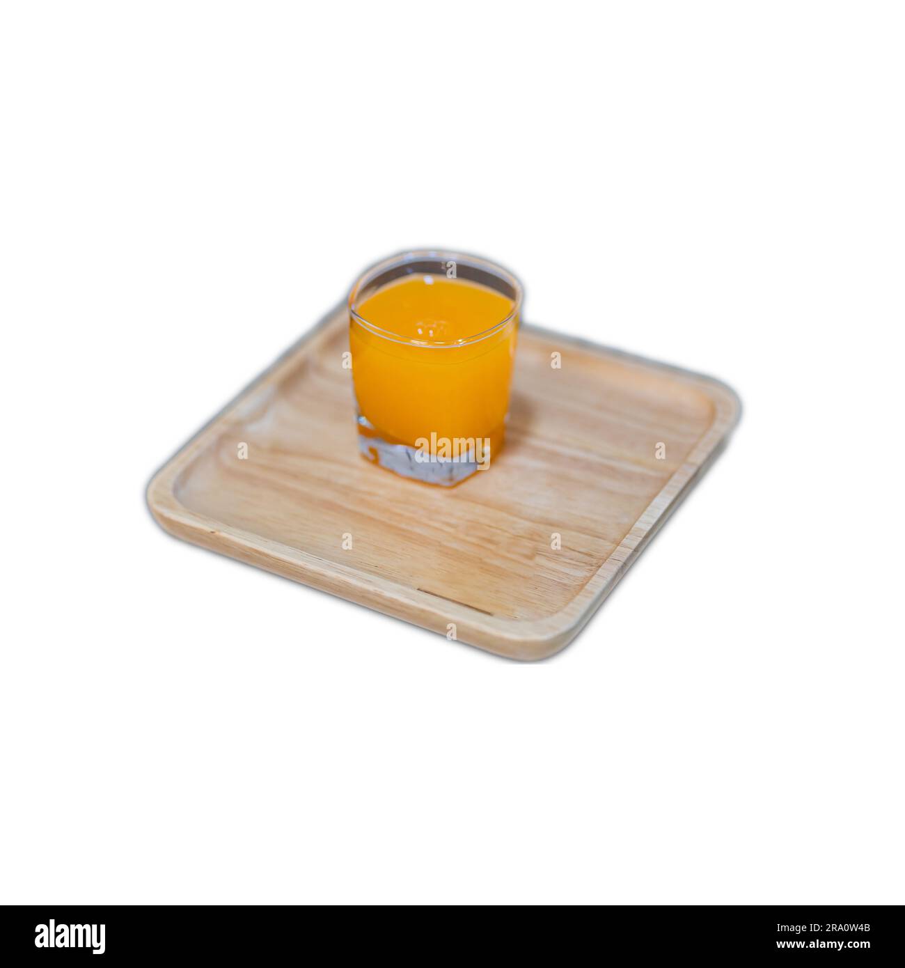 A clear glass of orange juice is placed on a wooden tray with a white ...