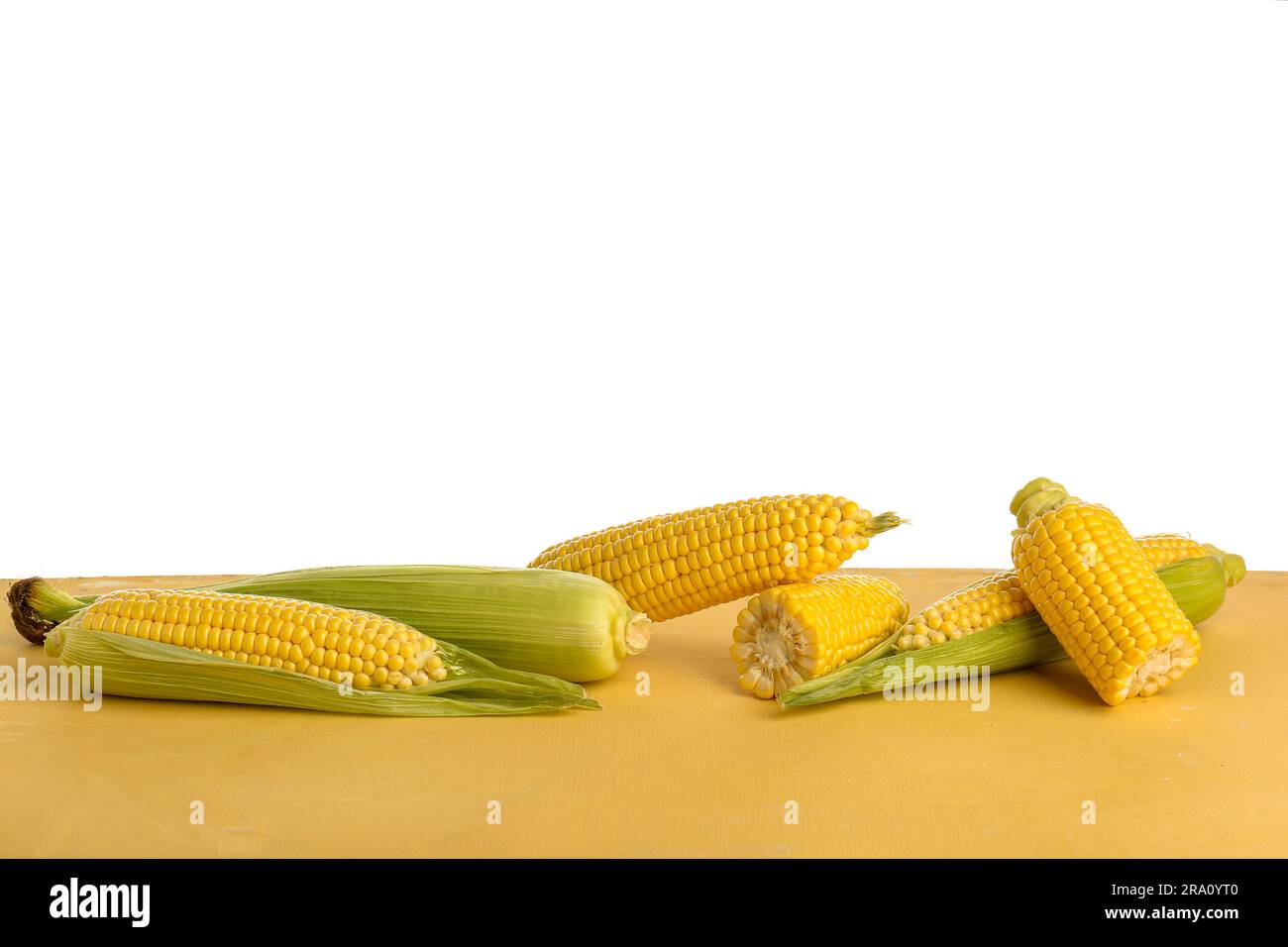 Fresh corn cobs on yellow table against white background Stock Photo ...