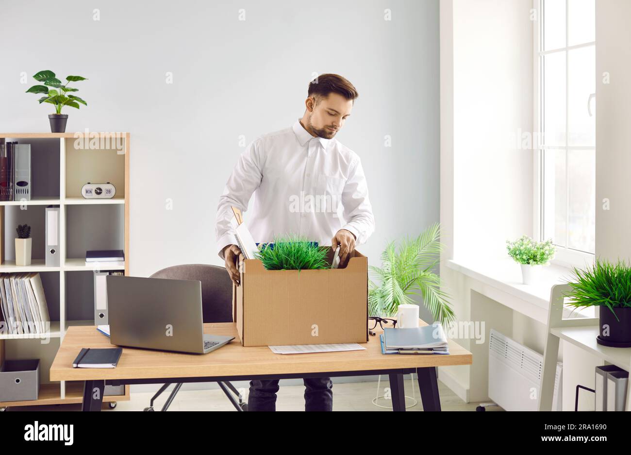 Fired employee standing by his office desk and packing his belongings ...