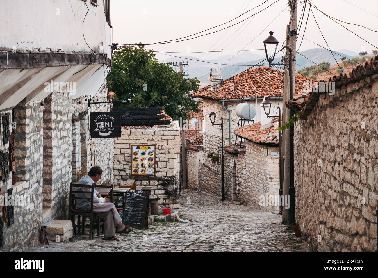 a man sits outside a restaurant inside the 13th century Berat Castle, a ...