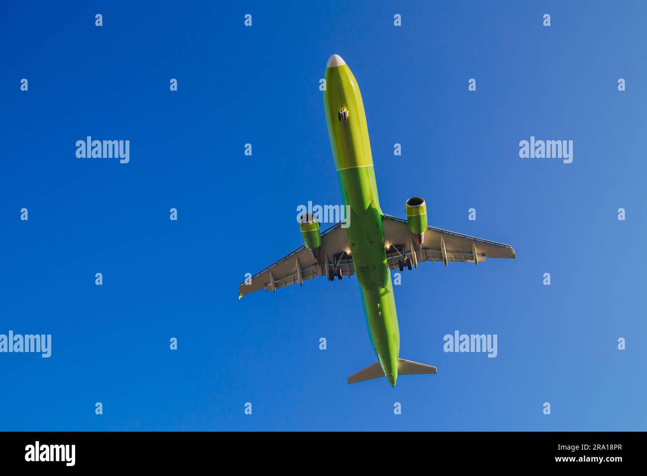 Passenger plane of yellow-green color flies in the blue sky, air ...