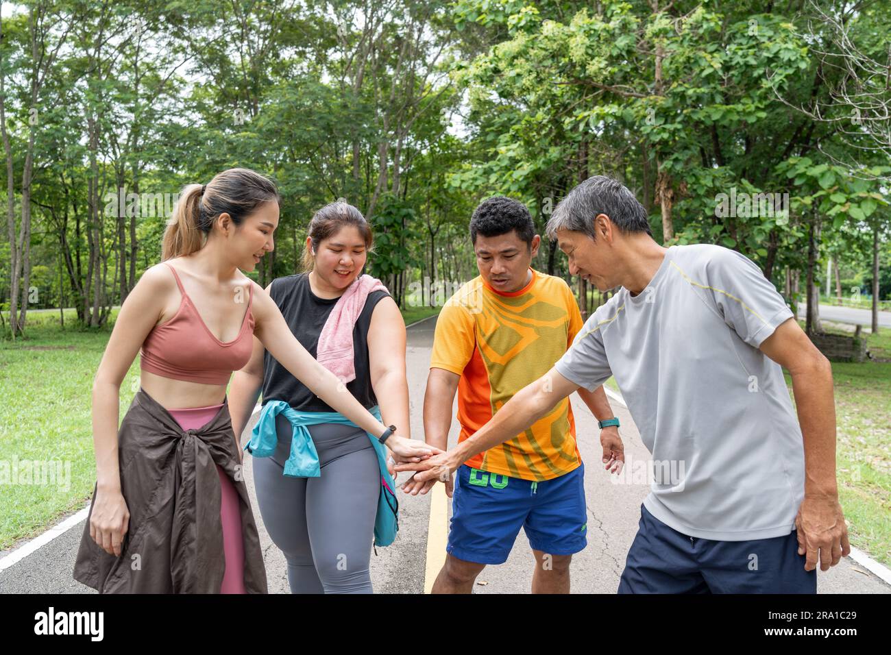 A group of 2 male and 2 female runners putting their hands togeter to ...
