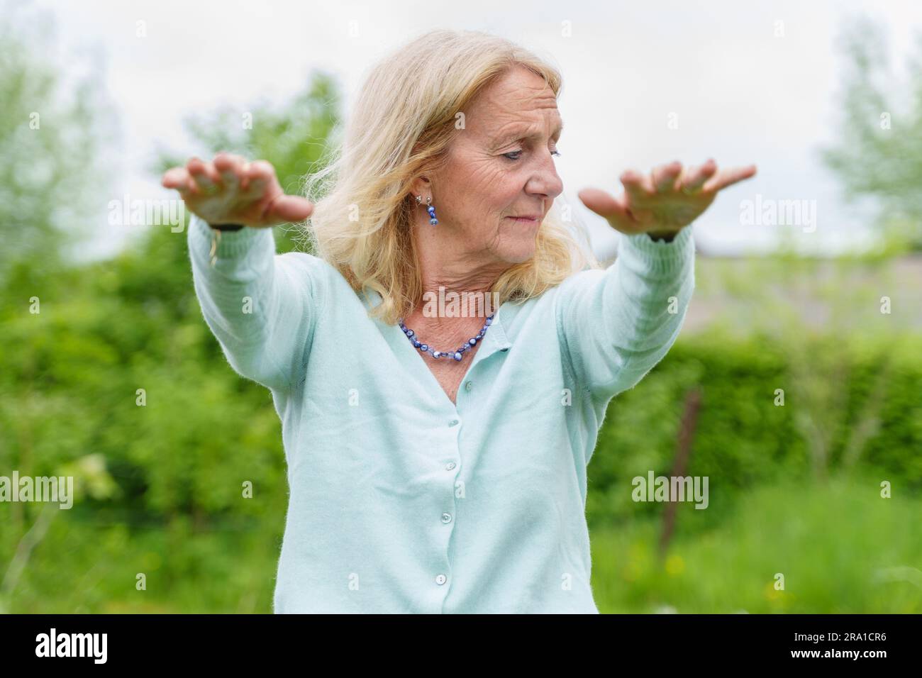 A senior blonde woman performs a stretching exercise in an outdoor ...