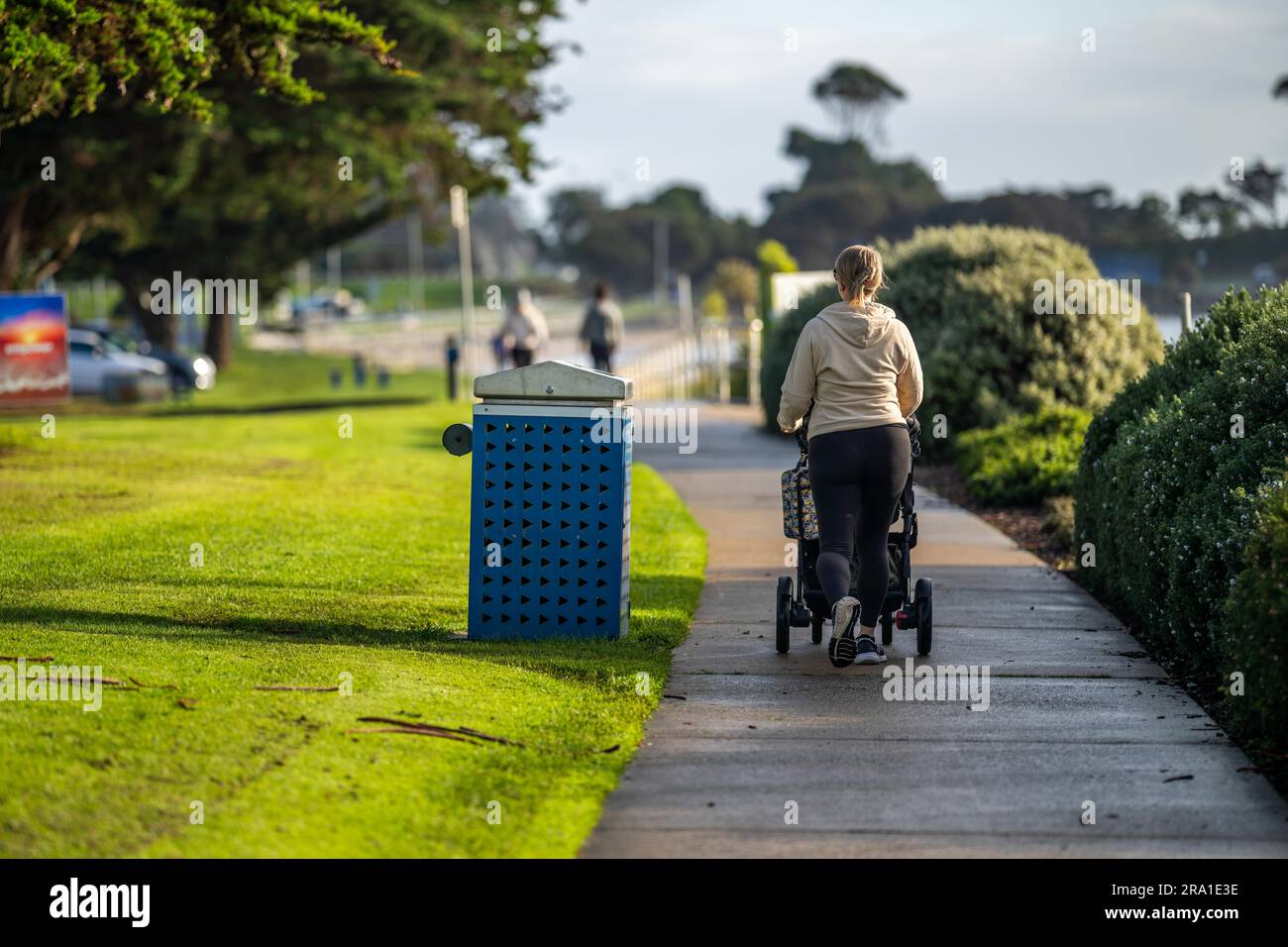 mother pushing a pram on a path by the ocean. young parent getting fit ...