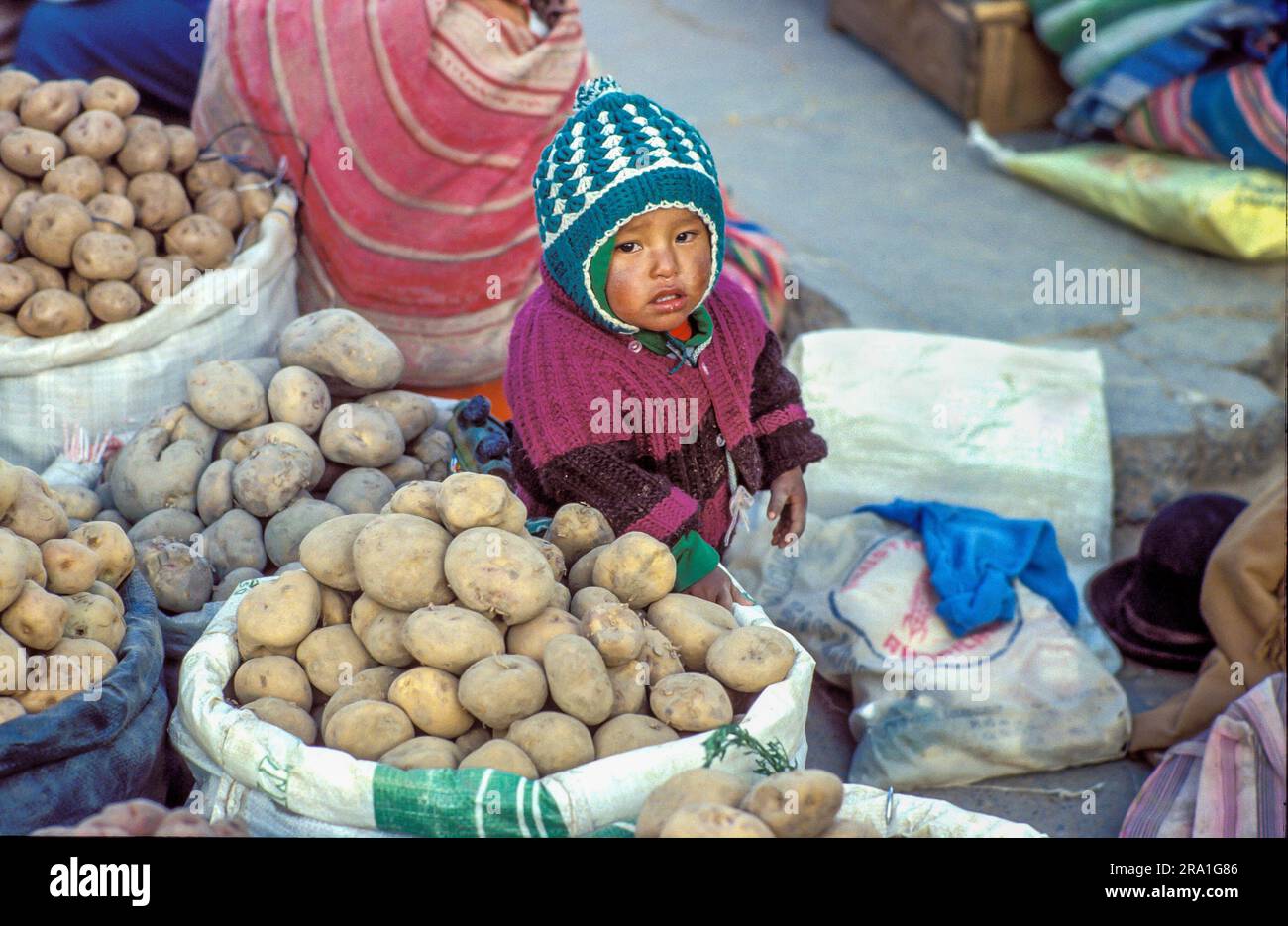Peru, littlel child sitting next to bags of potatoes that are sold on a ...