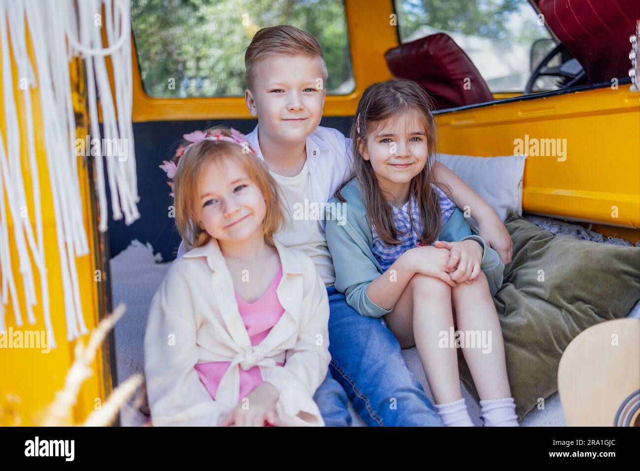Three cute little kids are sitting inside retro minivan in boho style ...