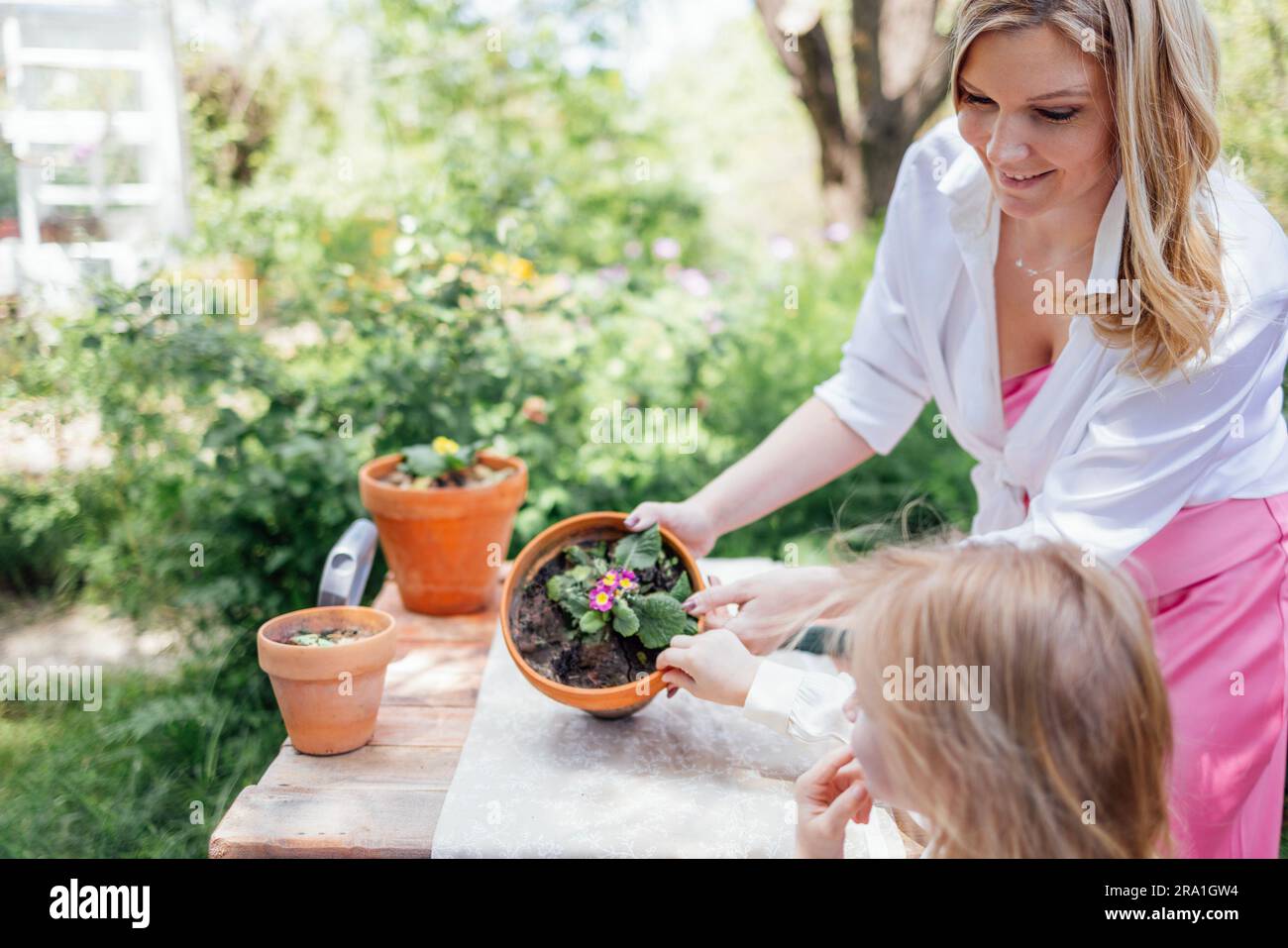 Little girl and her pretty blonde mom are planting flowers in clay pots ...