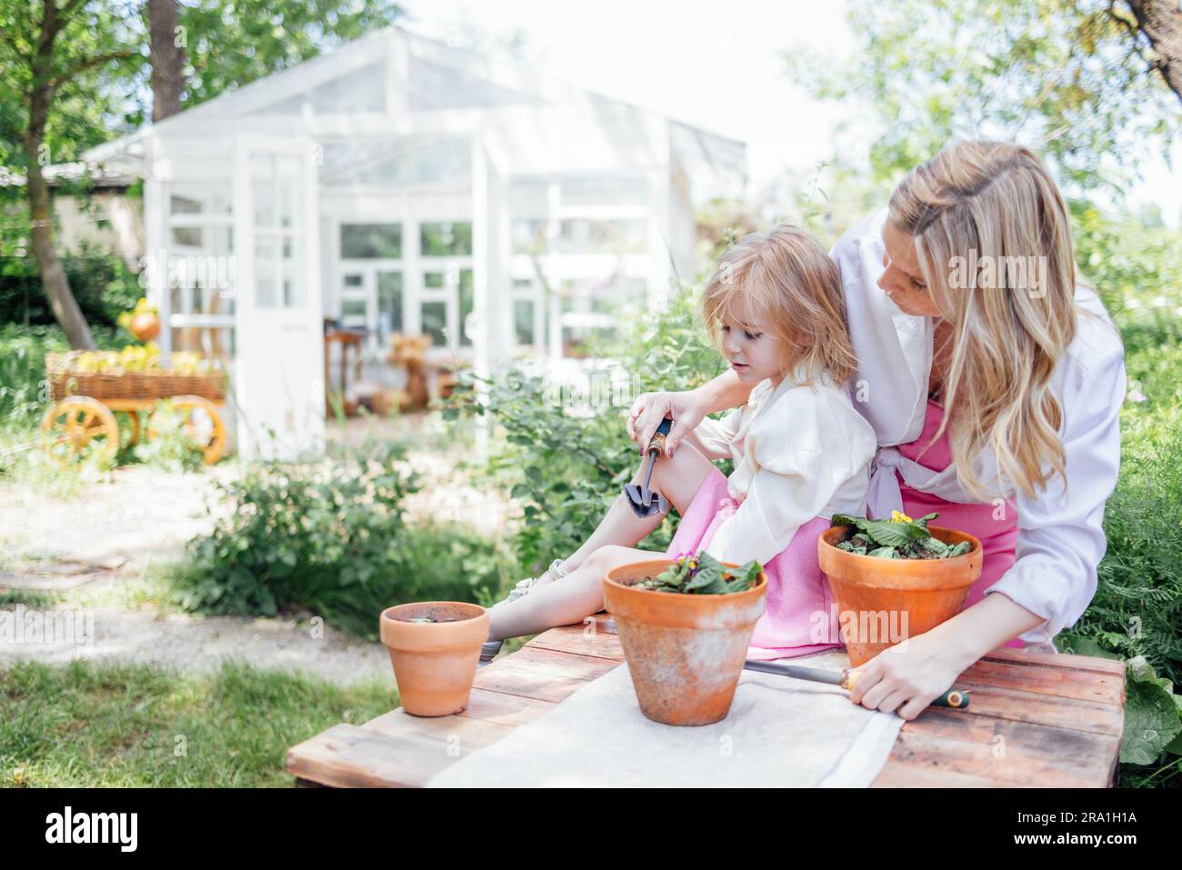 Little girl and her pretty blonde mom are planting flowers in clay pots ...