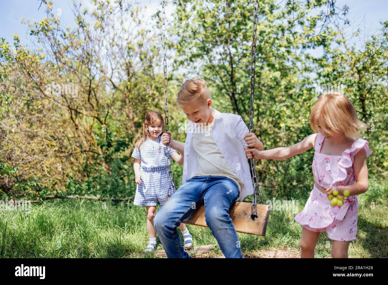 Pretty happy little girls in summer is rocking brother on swing Stock ...