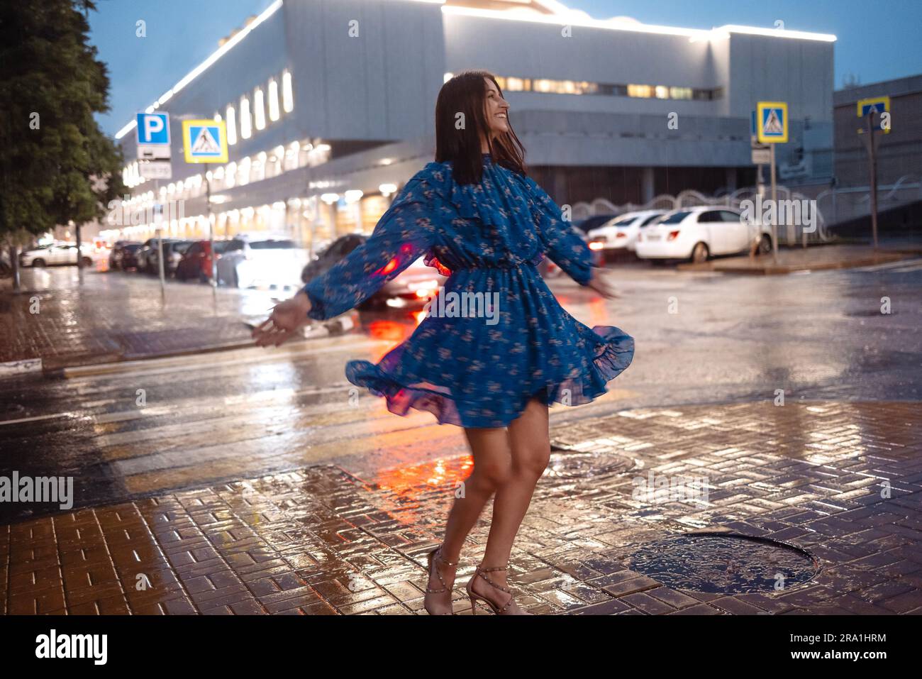 Beautiful brunette girl in blue dress laughs and dances in pouring rain ...