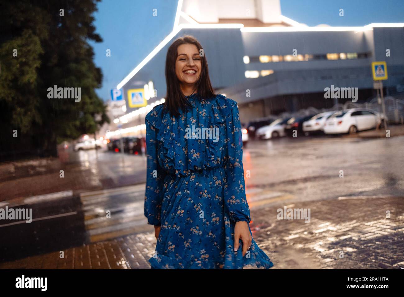 Beautiful brunette girl in blue dress laughs and dances in pouring rain ...