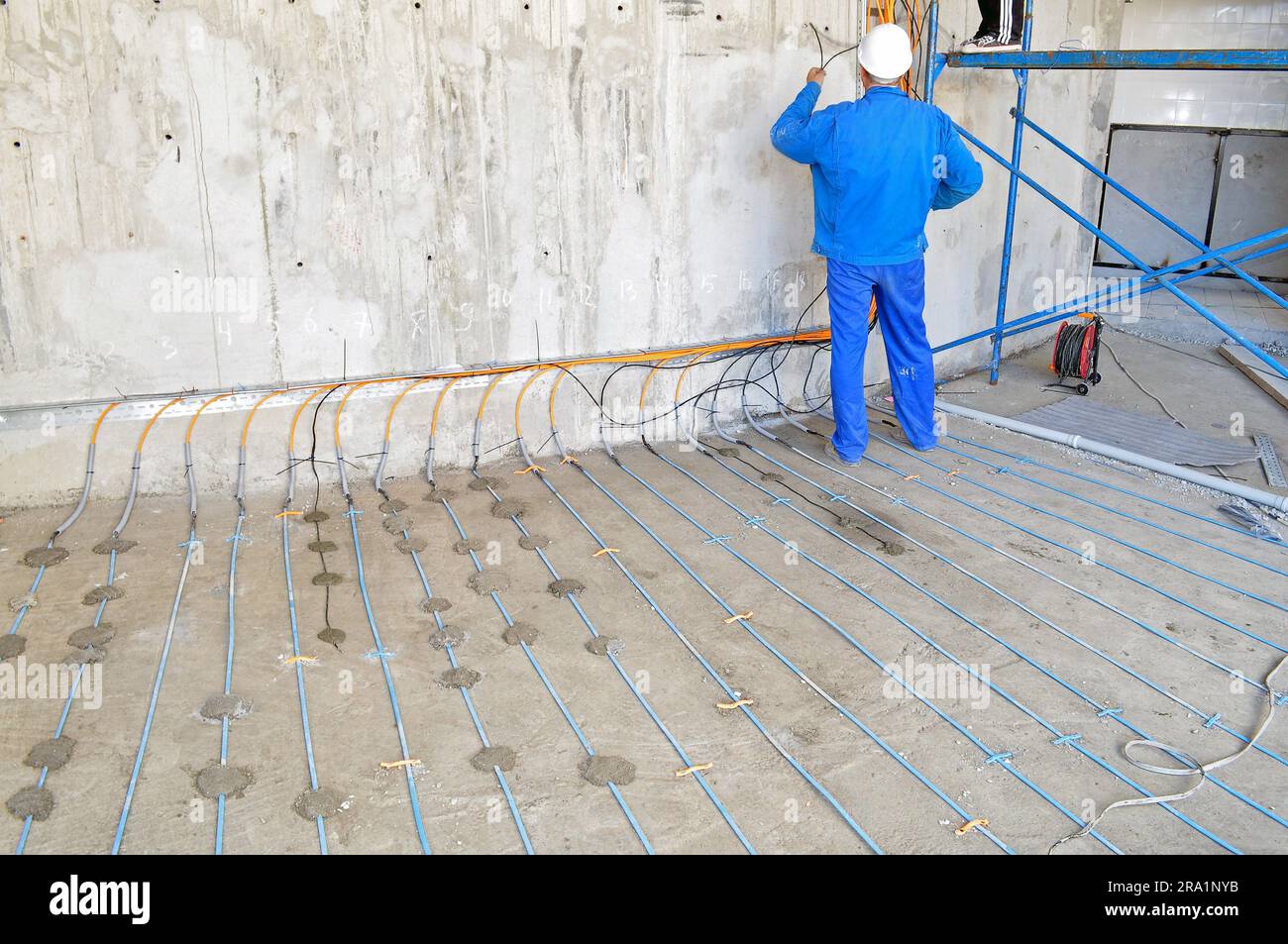A man wearing a blue uniform is seen installing an underfloor heating ...