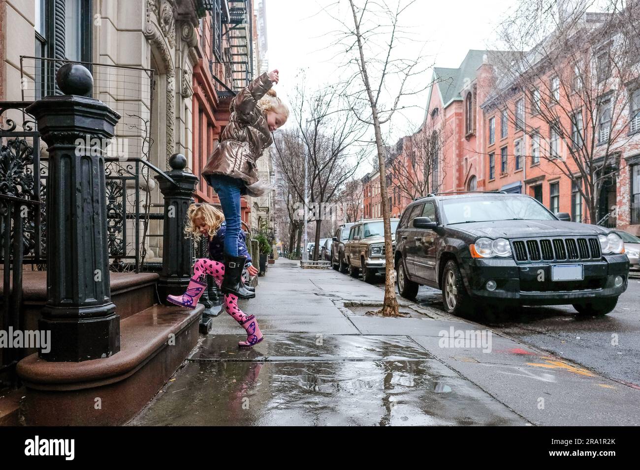young girls jumping off steps into puddle on rainy day on urban street ...