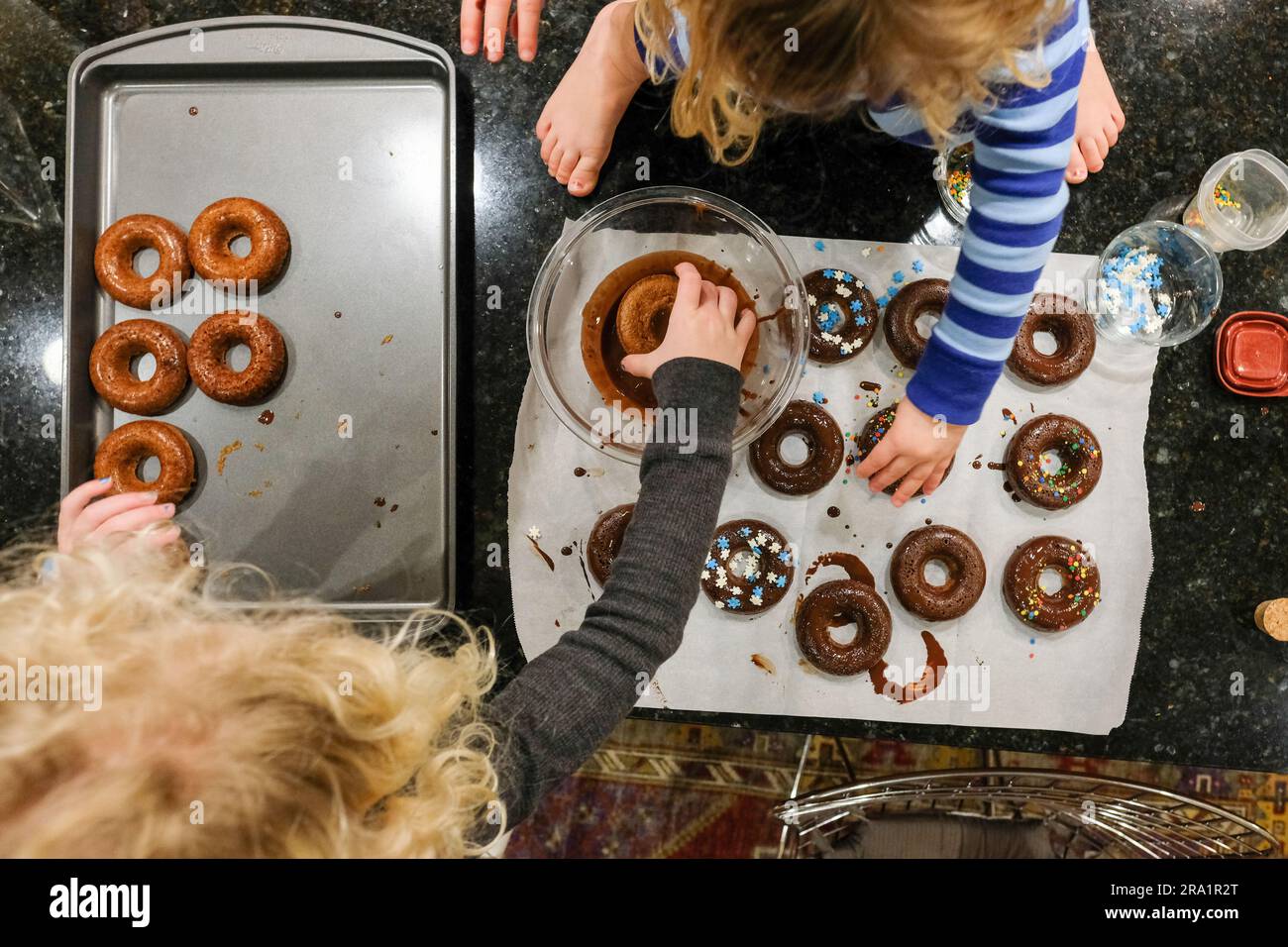Overhead view of children making donuts at home on kitchen counter ...