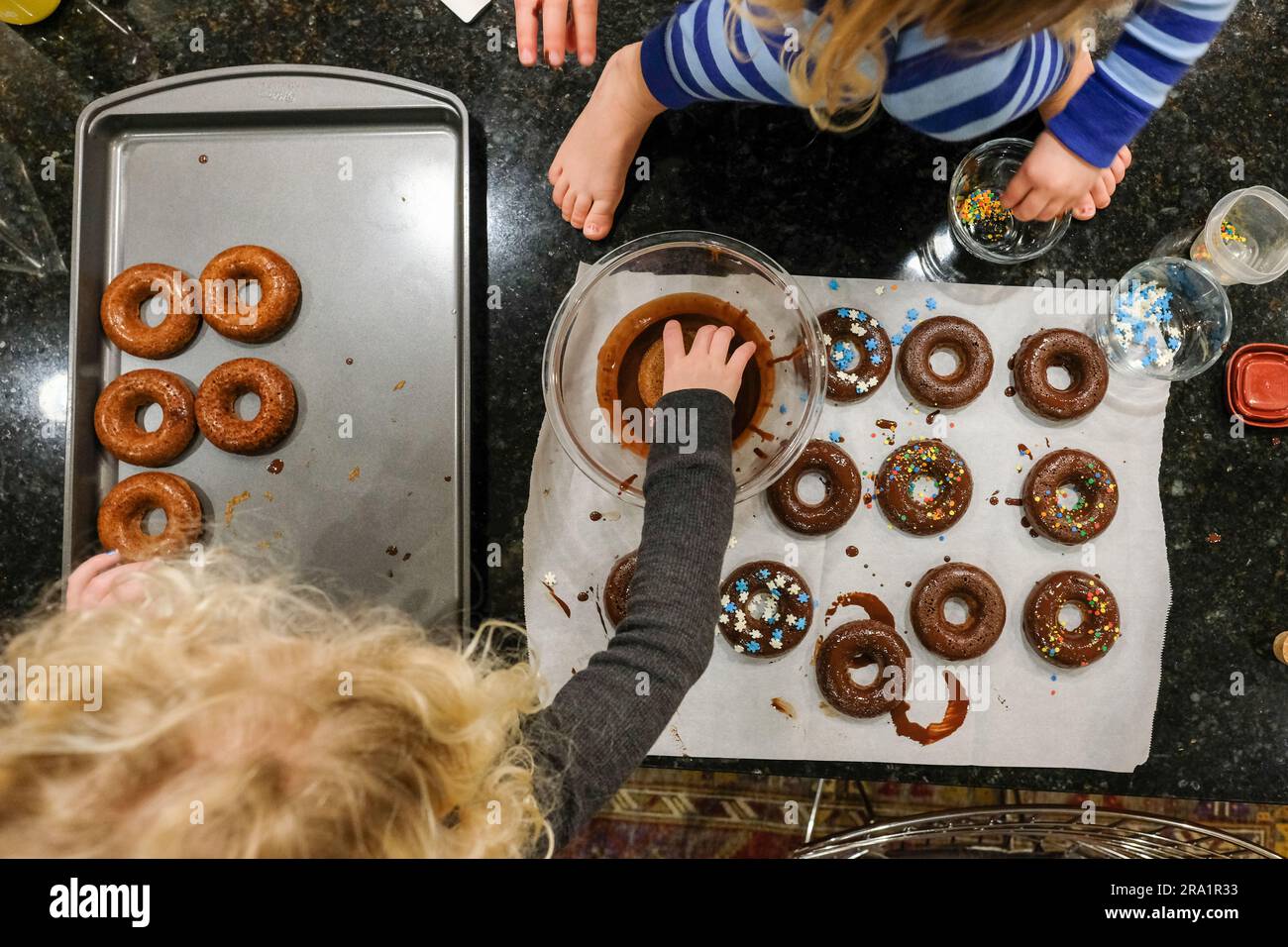 Overhead view of children making donuts at home on kitchen counter ...