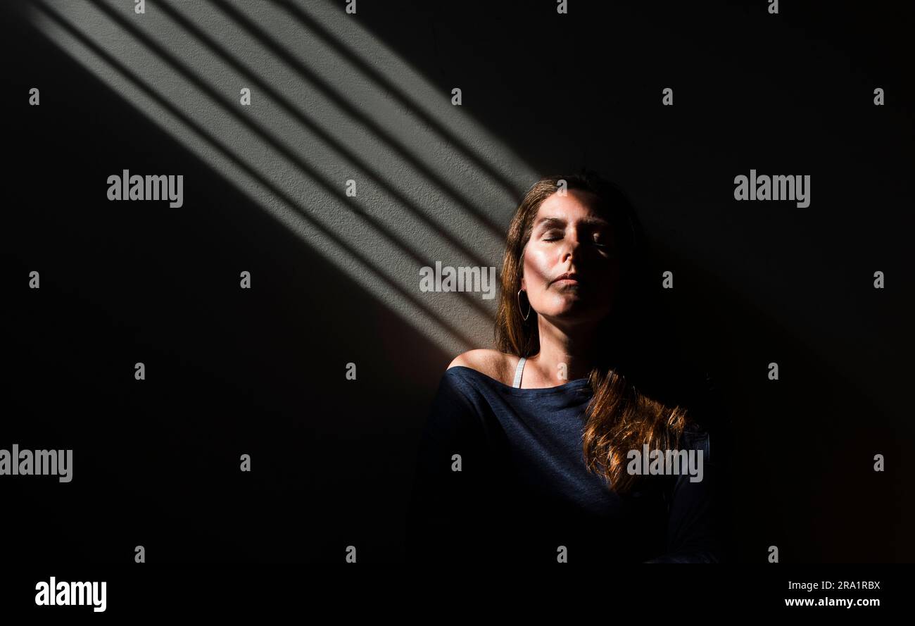 Portrait of a woman sitting in a patch of light with her eyes closed ...