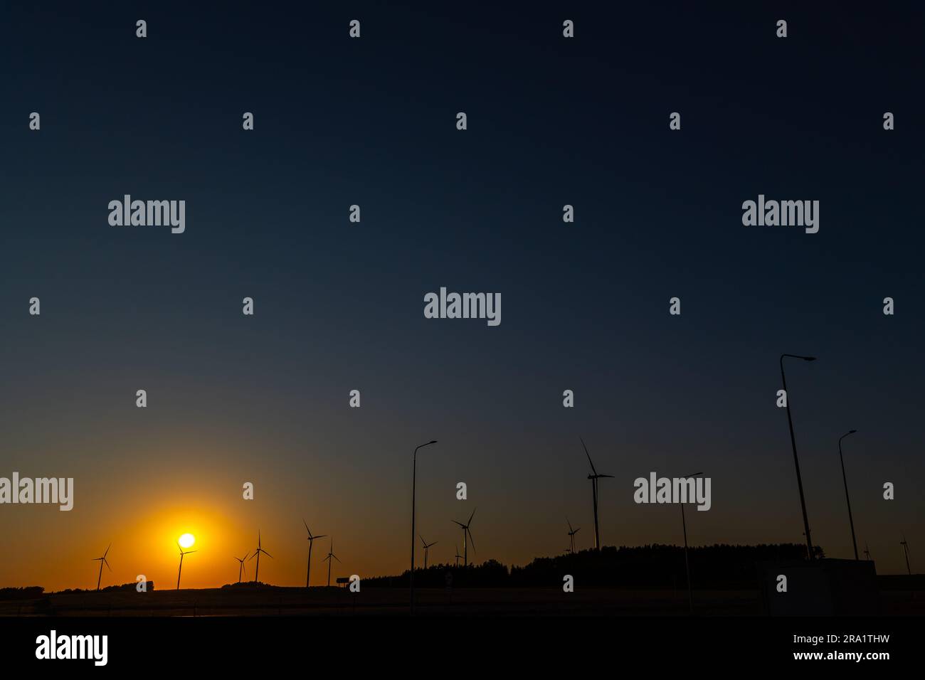 Many wind turbines spinning slowly against an orange sky during sunset ...