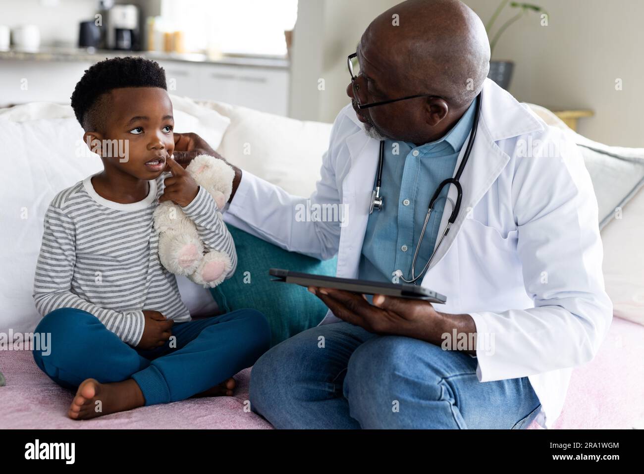 Senior african american male doctor using tablet talking to boy patient ...