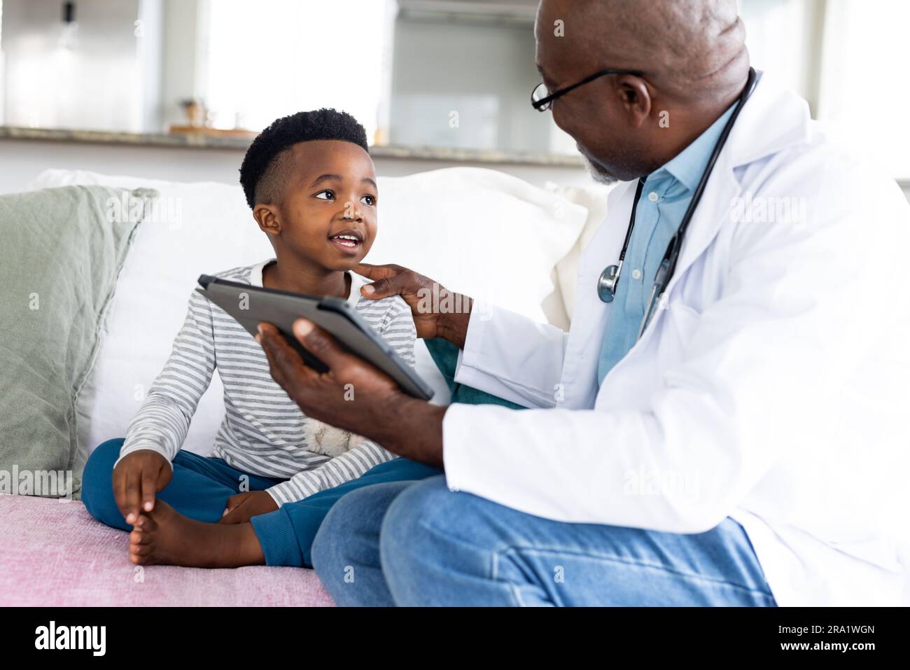 Senior african american male doctor using tablet talking to boy patient ...